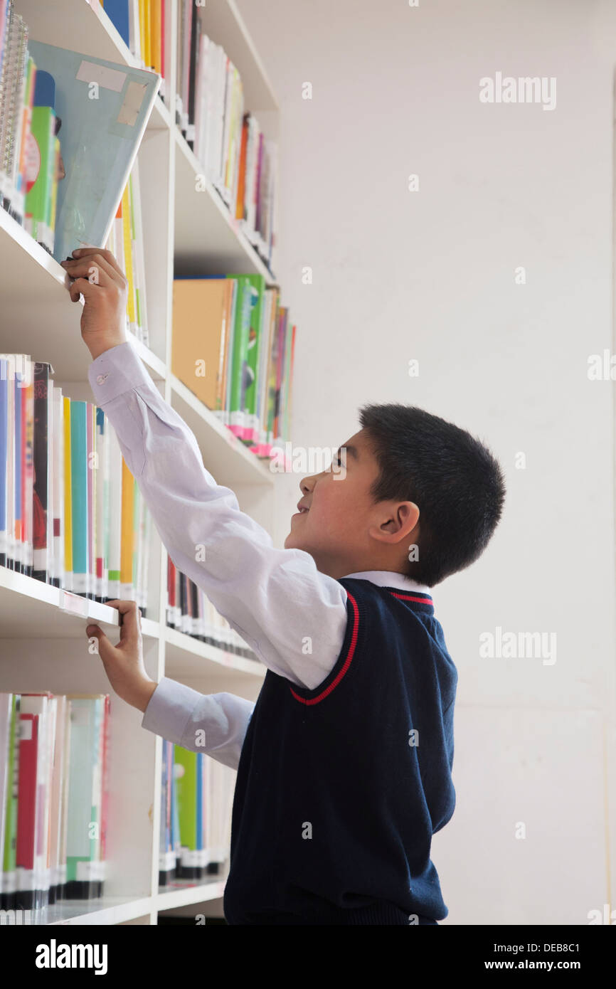 Schoolboy reaching for book off bookshelf Stock Photo - Alamy