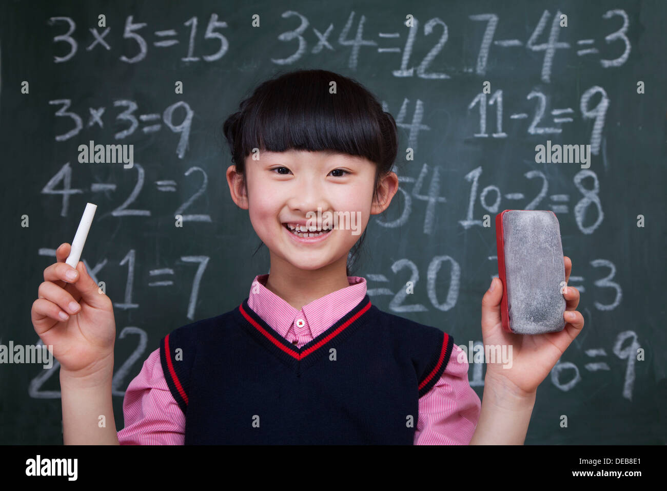 Portrait of schoolgirl in front of blackboard holding chalk and eraser ...