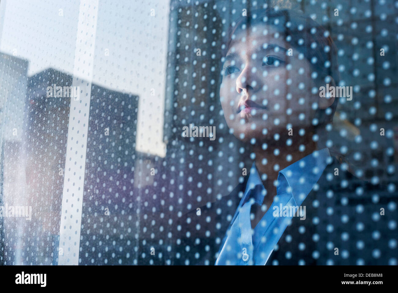 Businesswoman looking out through window, reflection of the city on the ...