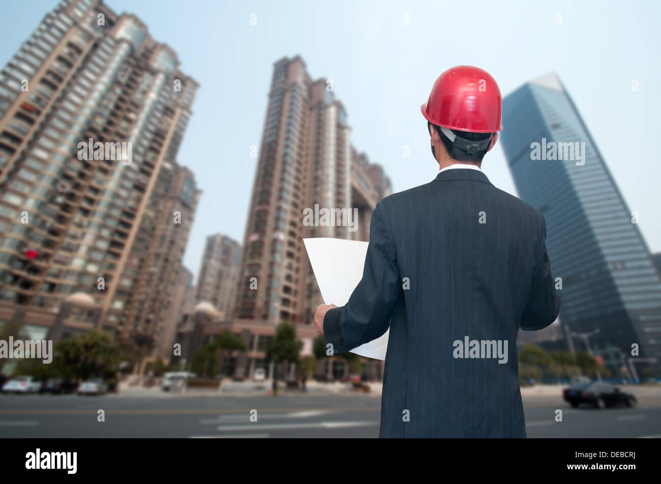Rear view of architect looking comparing housing project with building ...