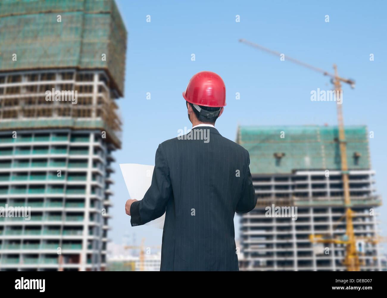Rear view of architect looking comparing housing project with building ...