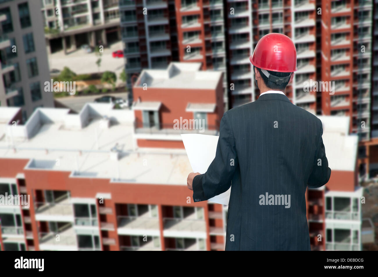 Rear view of architect looking comparing housing project with building ...
