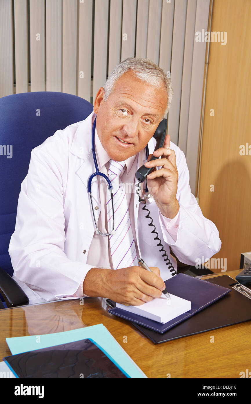 Senior doctor taking notes during phone call in his hospital office ... Senior doctor taking notes during phone call in his hospital office ...