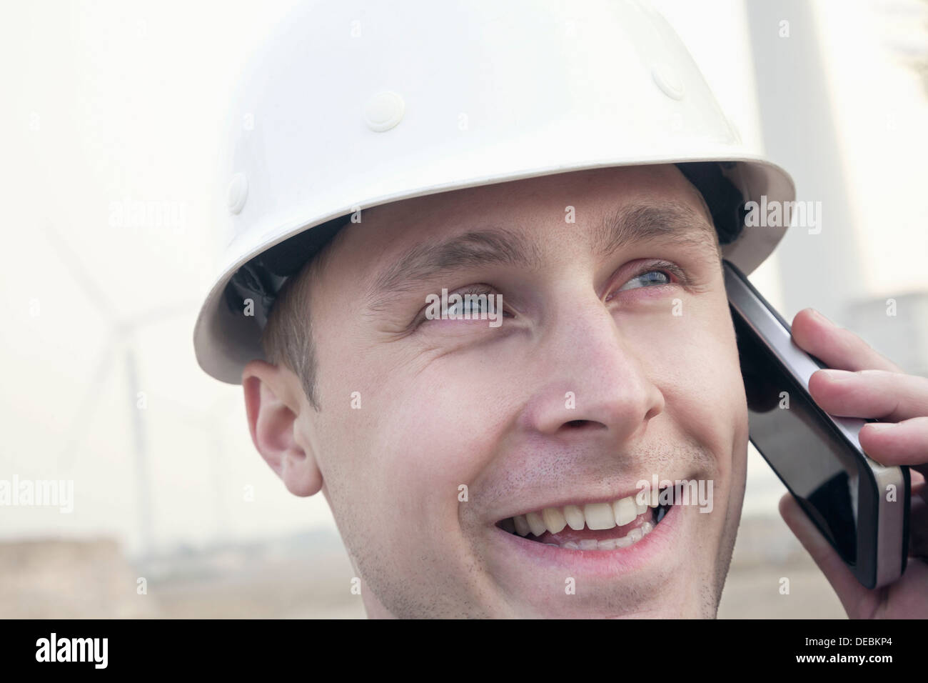 Young smiling male engineer in a hardhat on the phone beside a wind ...
