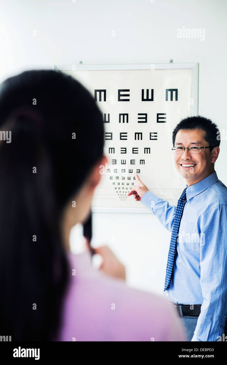 Optometrist administering an eye exam on a eye chart Stock Photo - Alamy