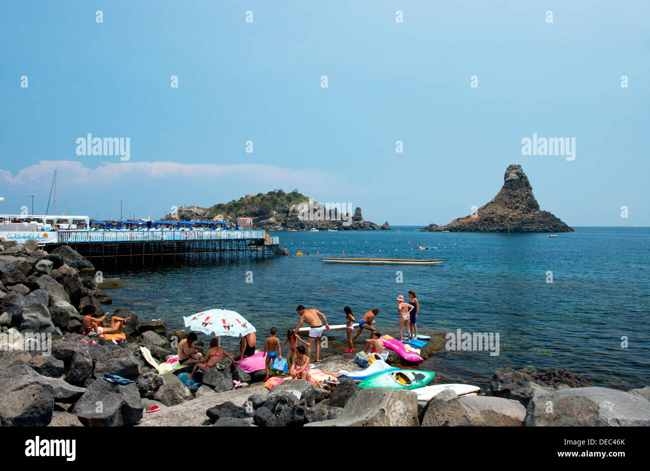 Sunbathers on rocks in Aci Trezza looking toward the Cyclops Islands ...