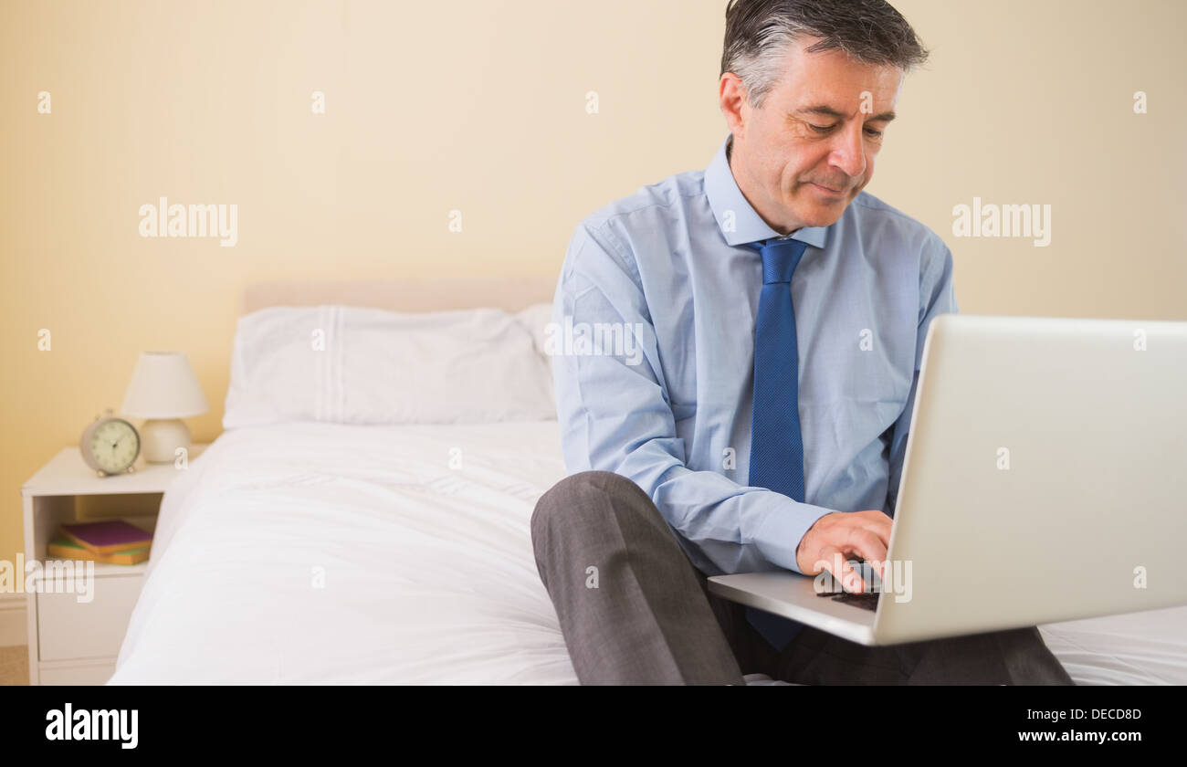 Concentrated man using a laptop sitting on a bed Stock Photo - Alamy