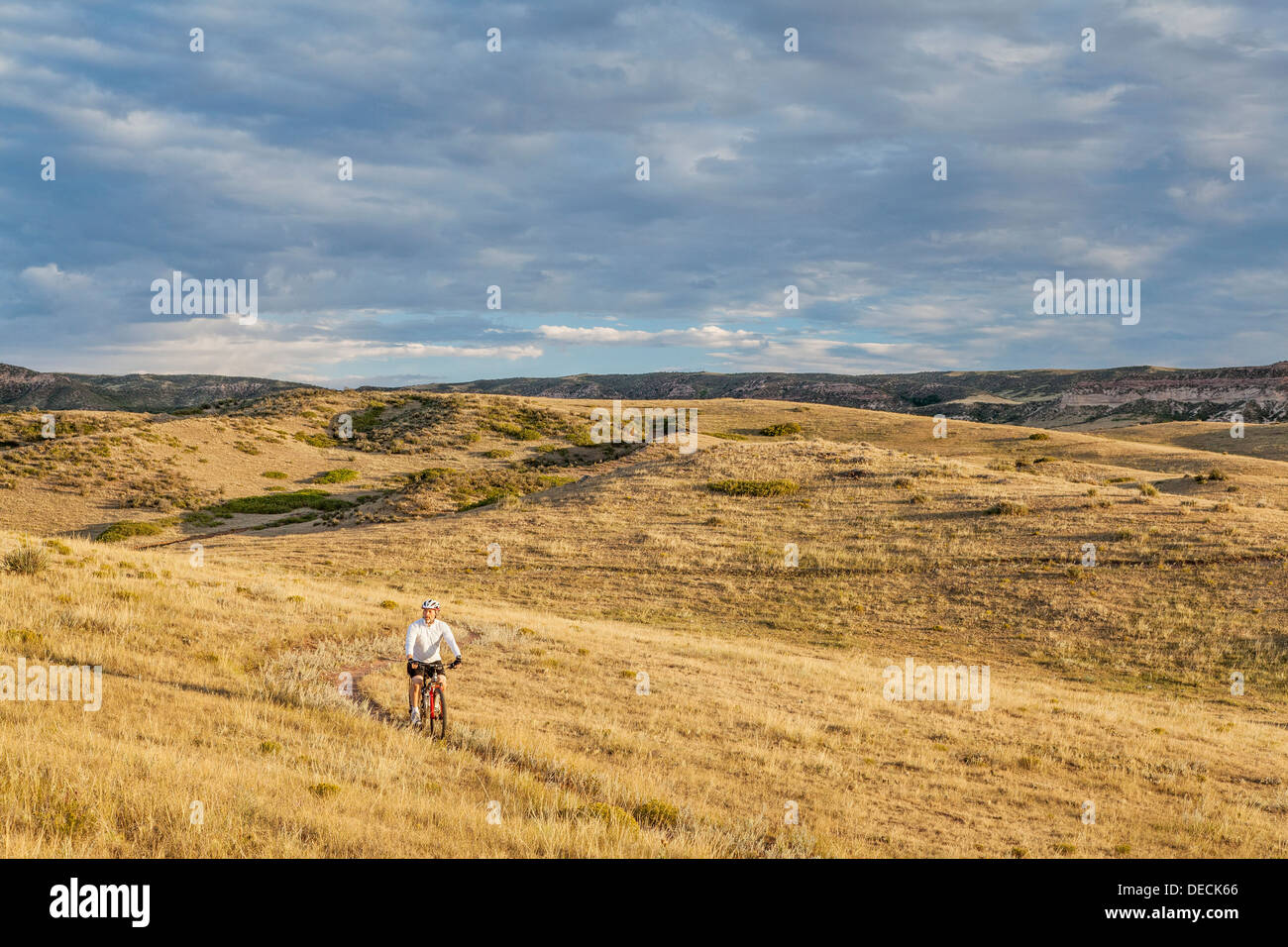 a lonely male biking over rolling prairie illuminated by sunrise at ...