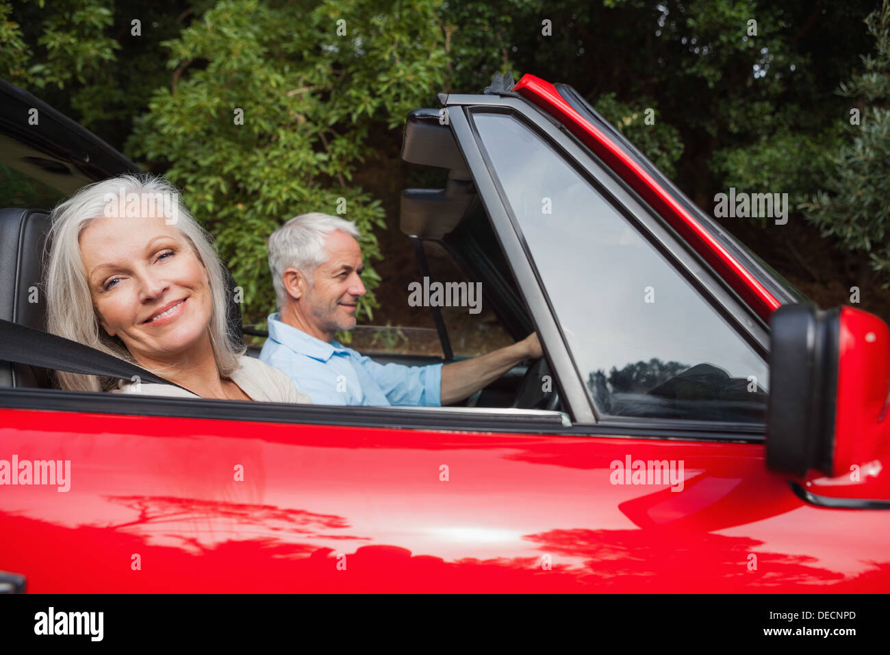 Side view of mature couple driving red convertible Stock Photo - Alamy