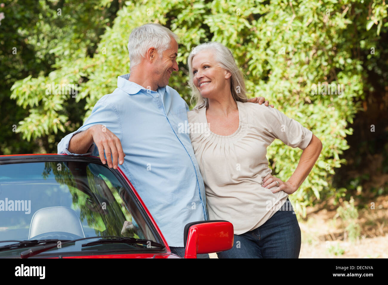 Smiling mature couple hugging by their red cabriolet Stock Photo - Alamy