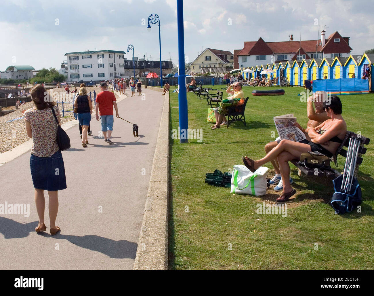 People walk along the seafront while others sit on benches and bask in ...