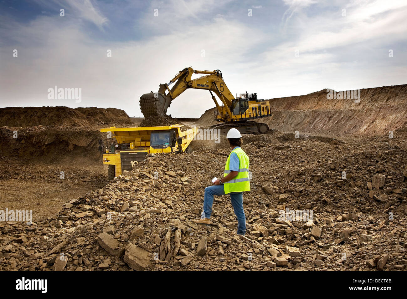 Supervisor overseeing gold mine operation in open cast surface pit with excavator and haul truck ...