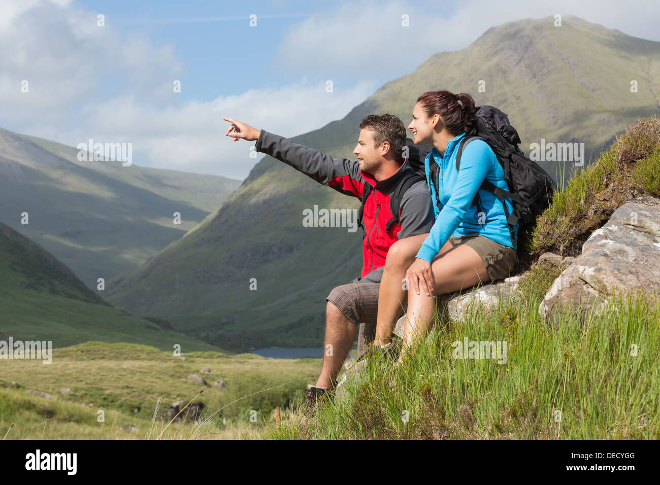 Couple taking a break after hiking uphill with man pointing Stock Photo ...