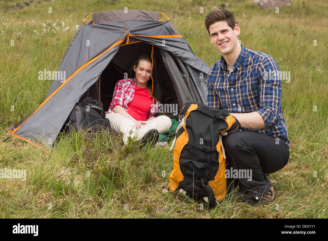 Smiling man packing backpack while girlfriend sits in tent Stock Photo ...