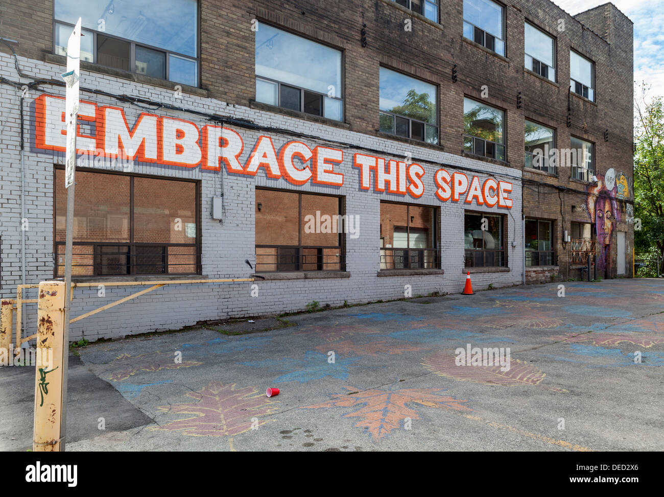 "Embrace this Space" sign on a building next to an empty car park decorated with drawings of ...