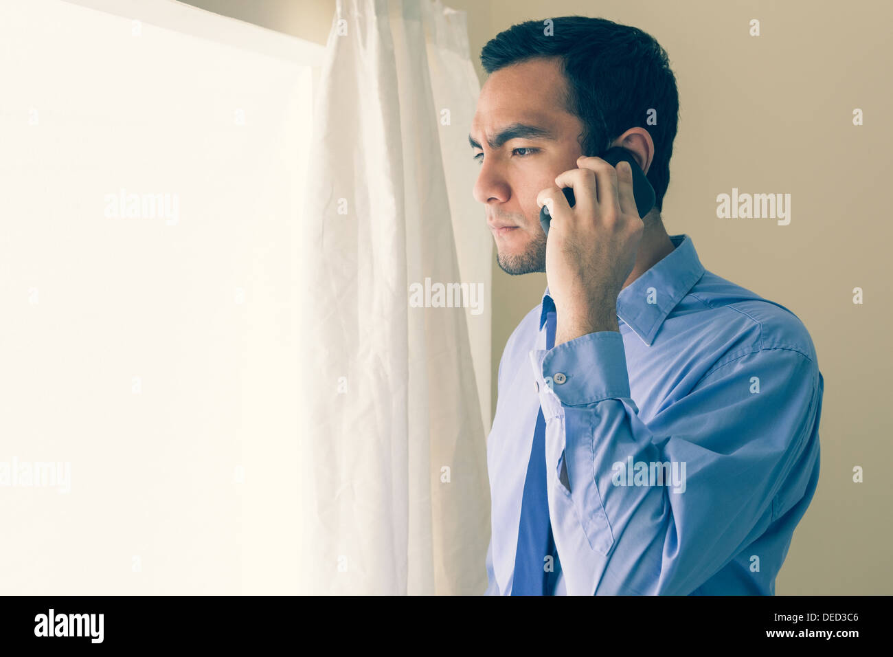 Irritated man calling someone with a mobile phone and looking out the ...