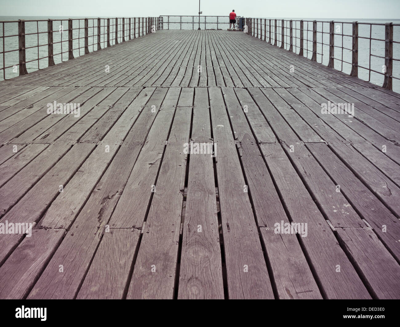Pier looking out to sea with a red fisherman at the end Stock Photo - Alamy
