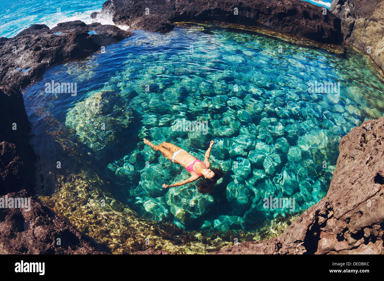 Attractive young woman floating in beautiful ethereal natural pool ...