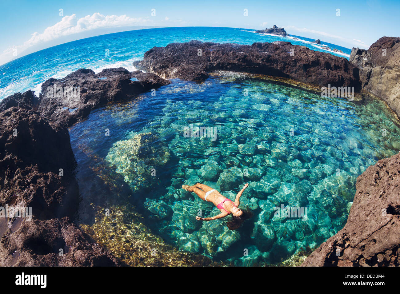 Attractive young woman floating in beautiful ethereal natural pool ...