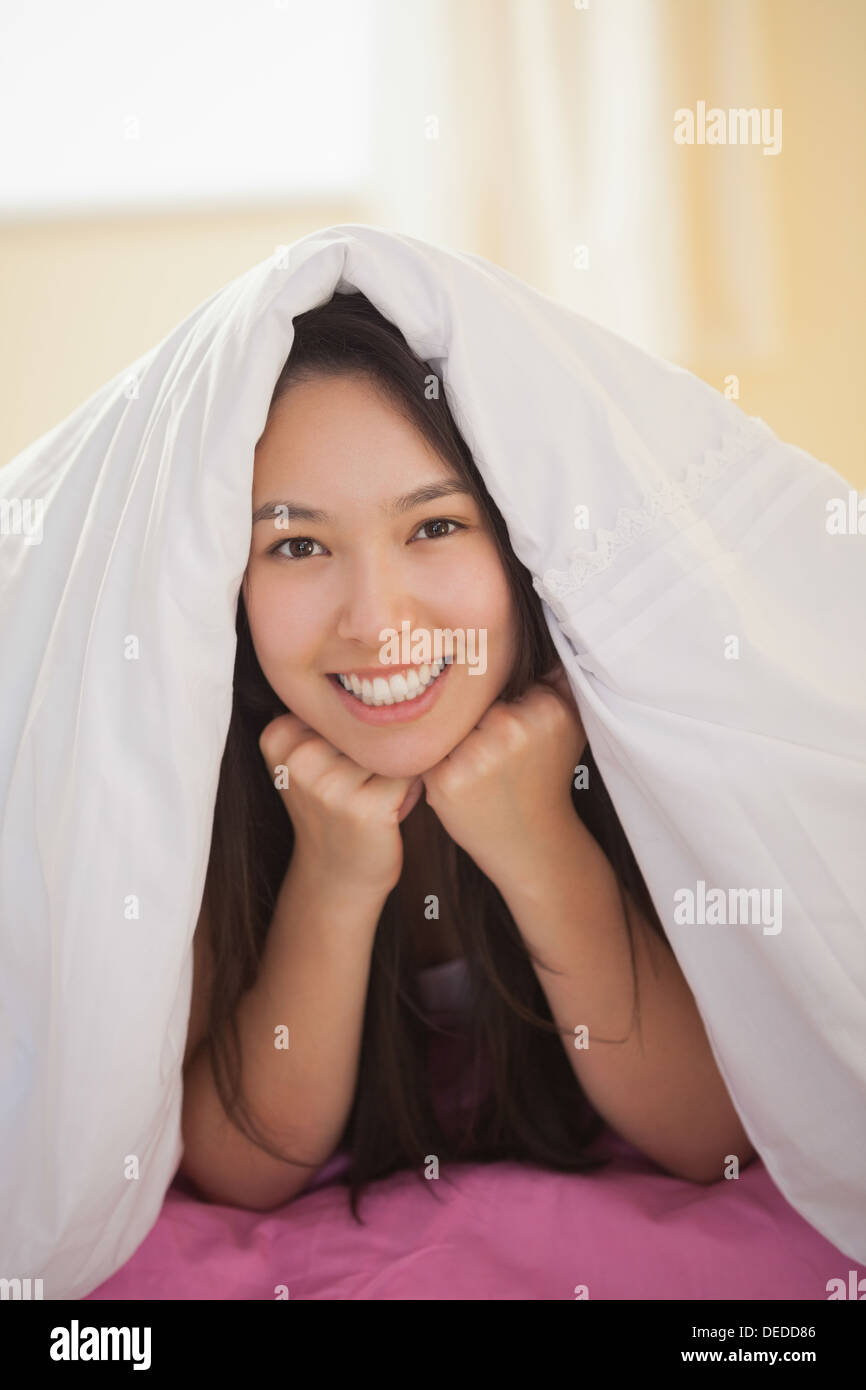 Cute young asian woman under her duvet smiling at camera Stock Photo ...