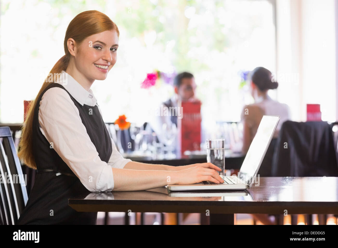 Happy businesswoman typing on laptop while smiling at camera Stock ...