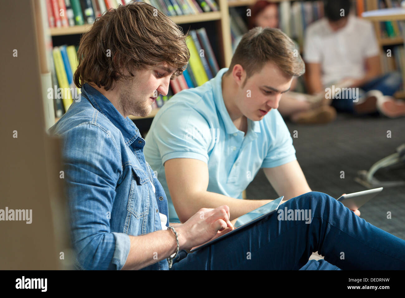 Group of two male boy students using tablet computers in a college ...