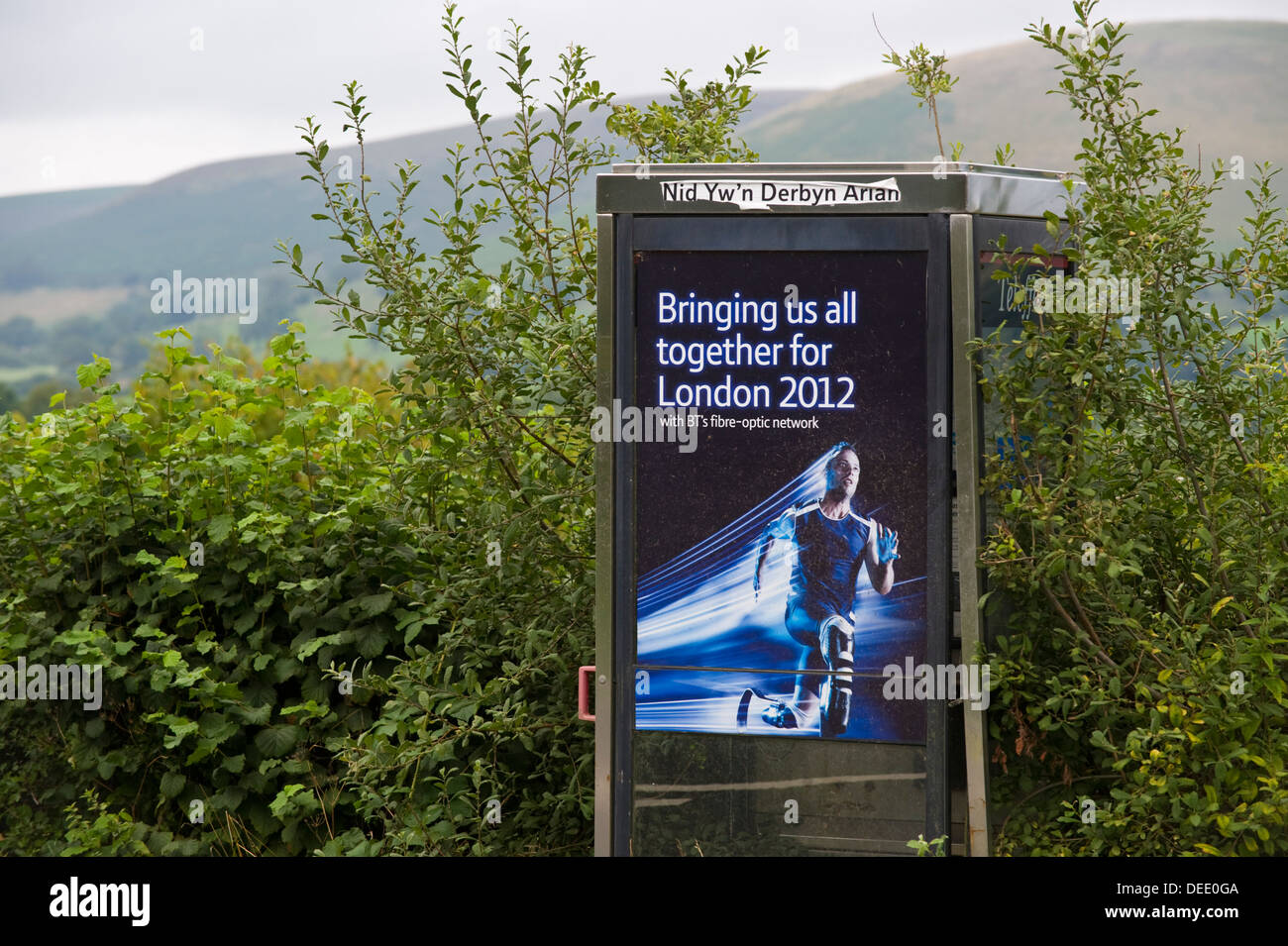 Derelict overgrown BT phone box advertising BT's fibre-optic broadband ...