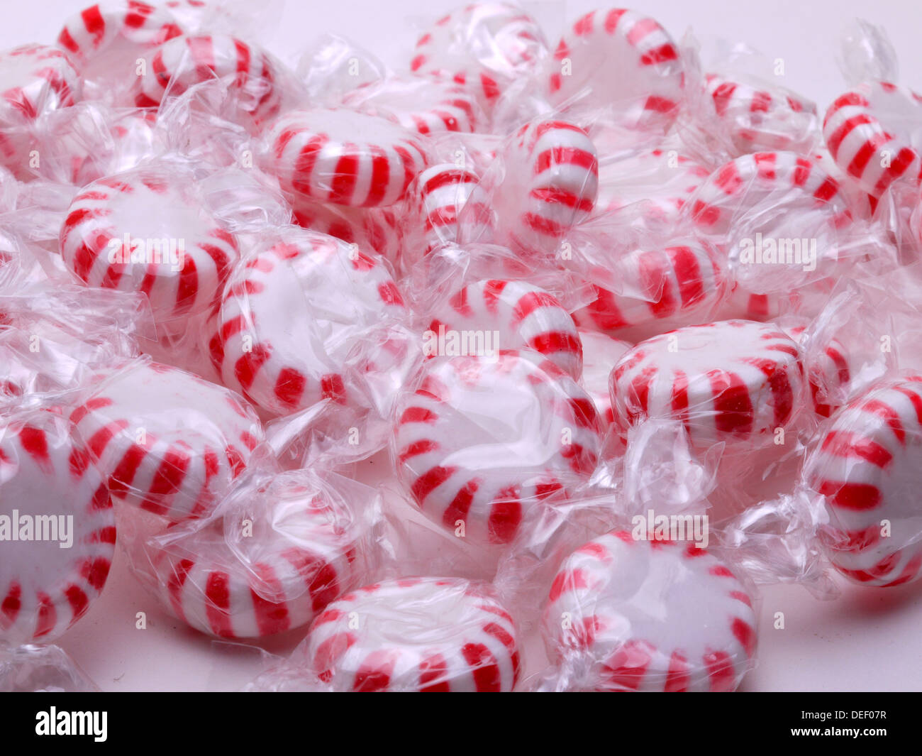 A handful of red and white stripe peppermints are laying on a white ...