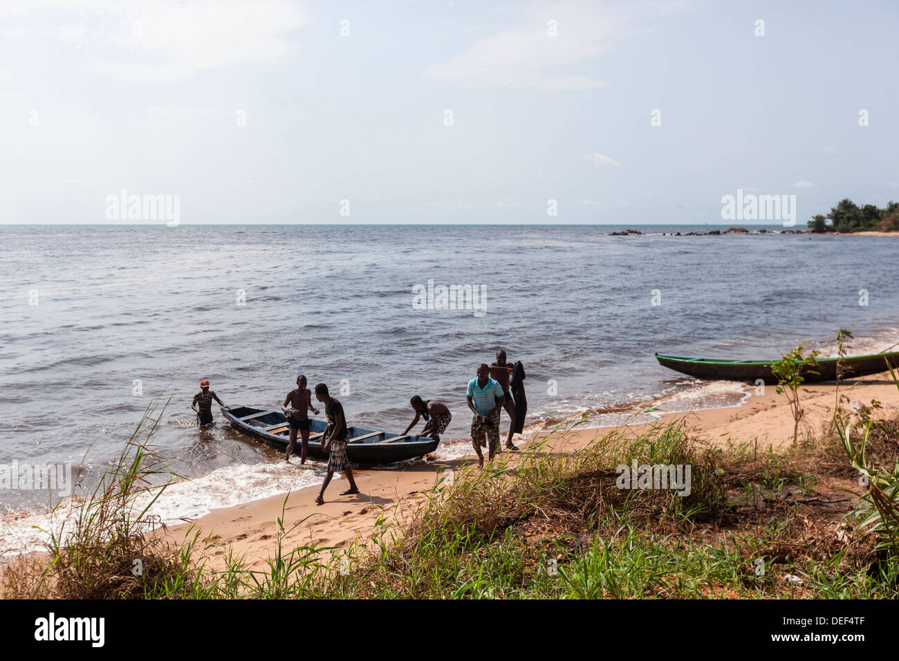 Africa, Cameroon, Kribi. Men pulling traditional wooden boat into shore ...