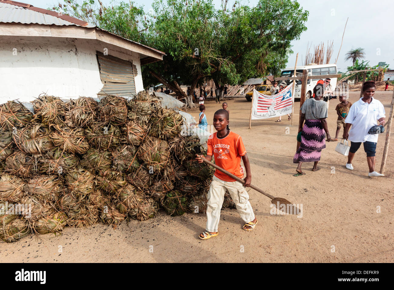 Africa, Liberia, Monrovia. People walking by bundles of dried pandanus ...