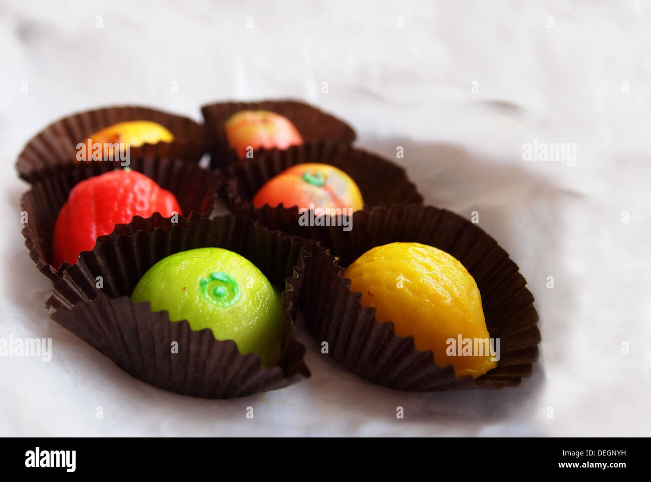 Six colorful pieces of marzipan fruit shapes in white tissue paper ...