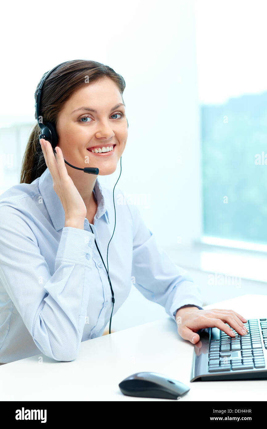 Portrait of young operator with headset looking at camera at workplace ...