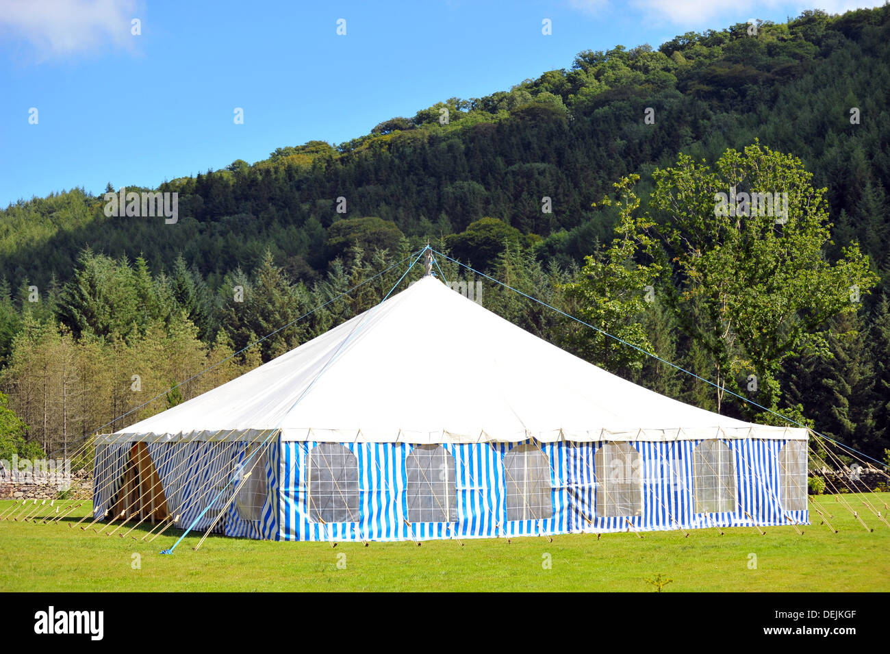 A large white marquee erected on grass surrounded by tree covered hills ...