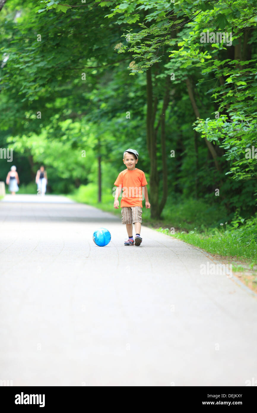 Boy young kid playing with ball kicks running towards ball in park ...