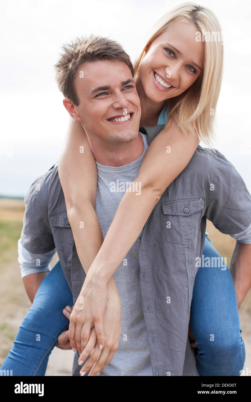 Happy young man giving piggyback ride girlfriend on field Stock Photo - Alamy