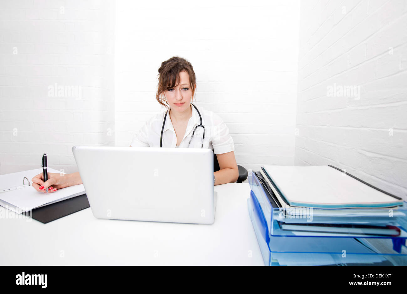 Young female doctor with laptop writing notes on desk clinic Stock ...