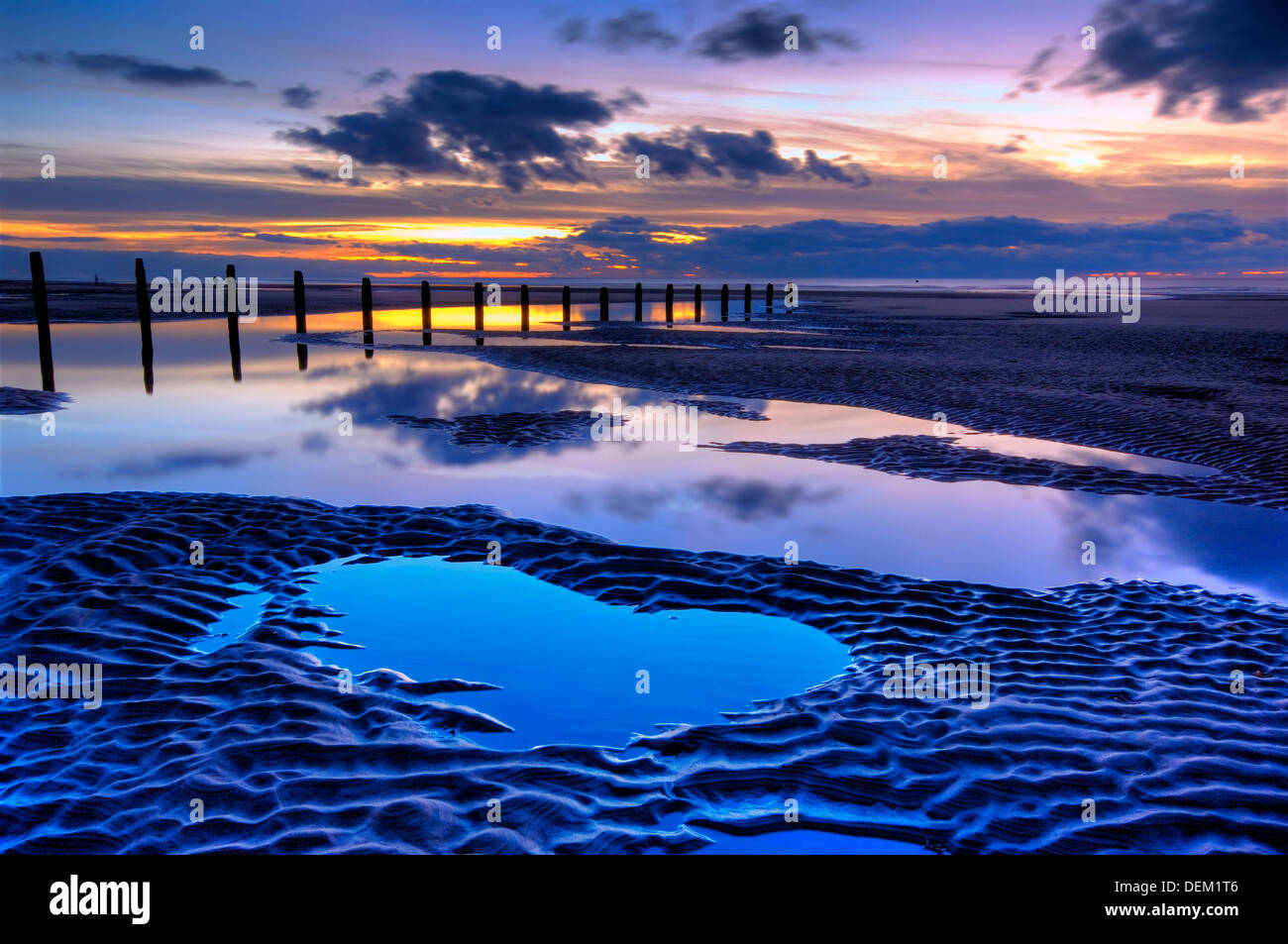 beach and wooden groyne at sunset, with large pools of water and cloud ...
