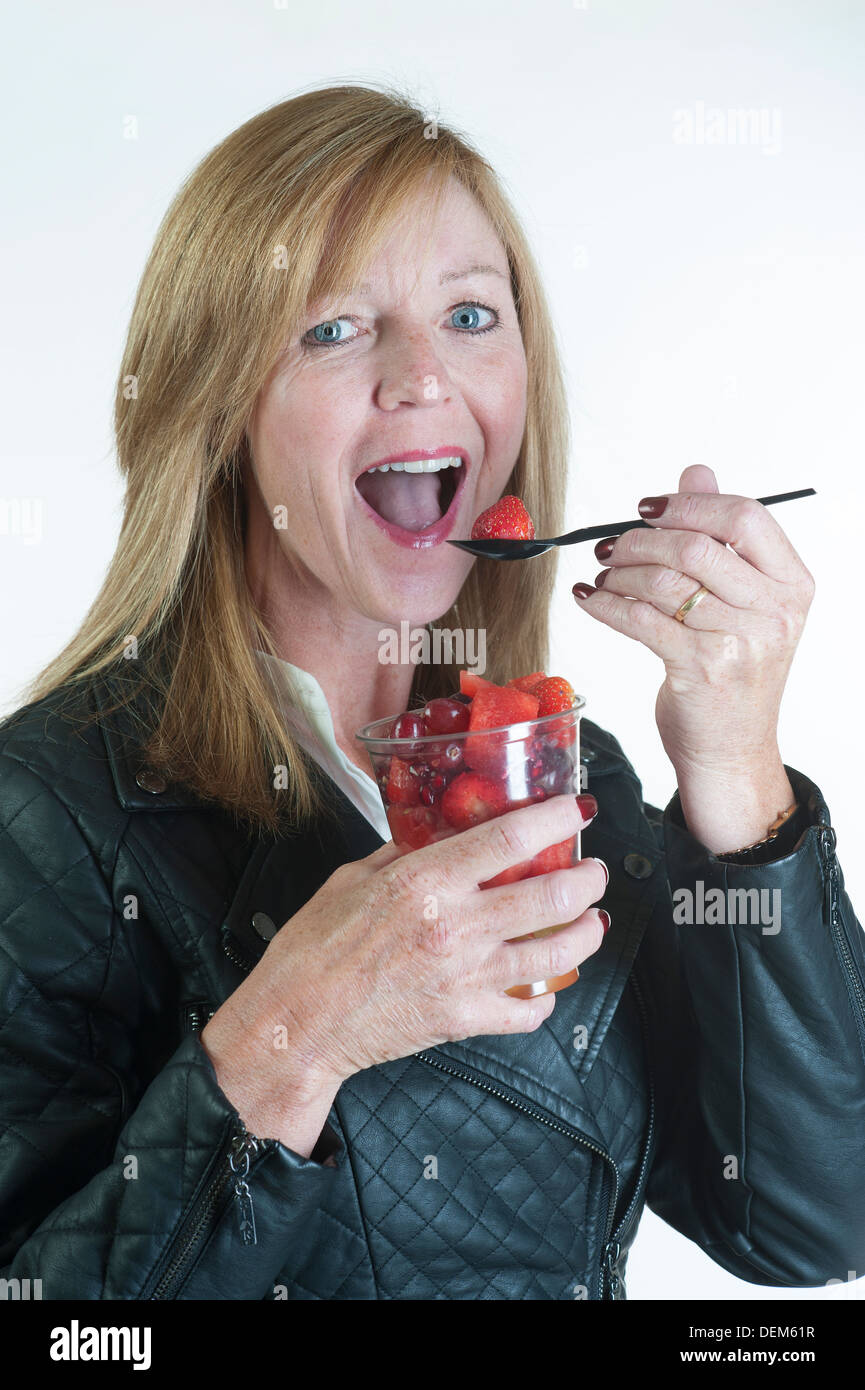 Woman eating fresh fruit salad from plastic cup using a plastic spoon ...
