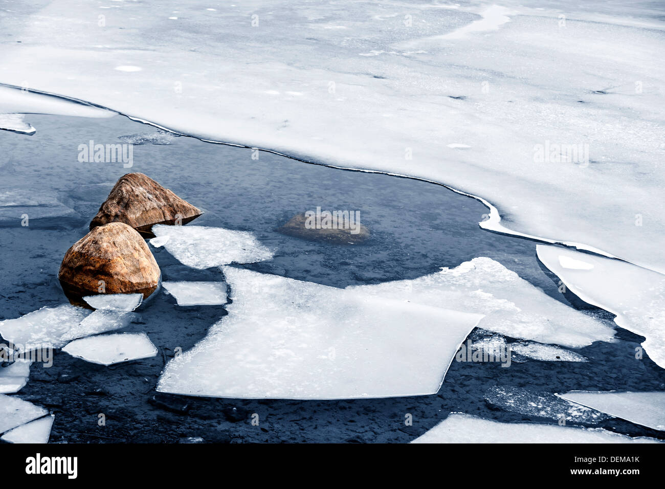 Broken ice floating on water at cold lake shore with rocks in winter ...