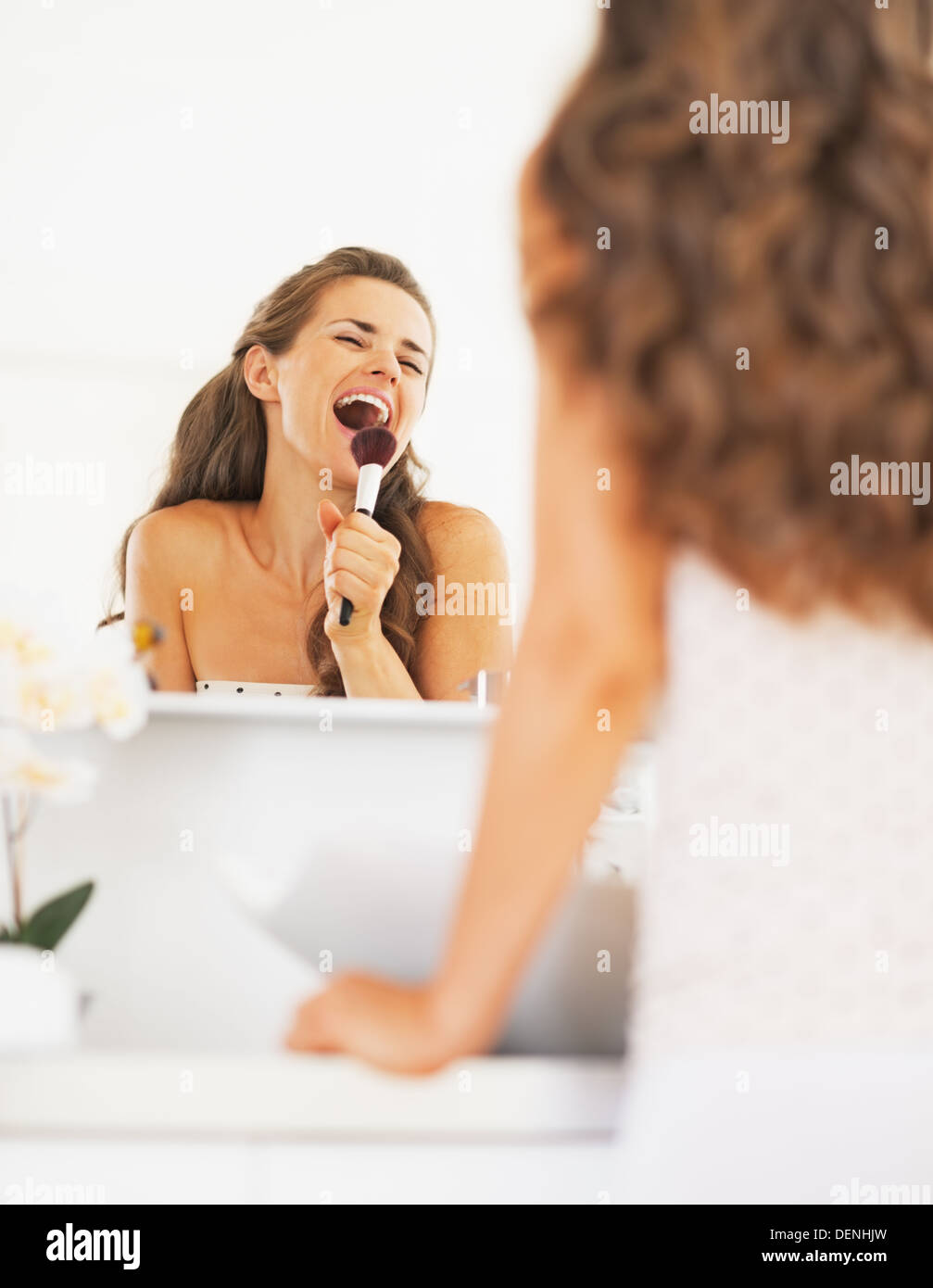 Happy young woman singing in makeup brush in bathroom Stock Photo - Alamy