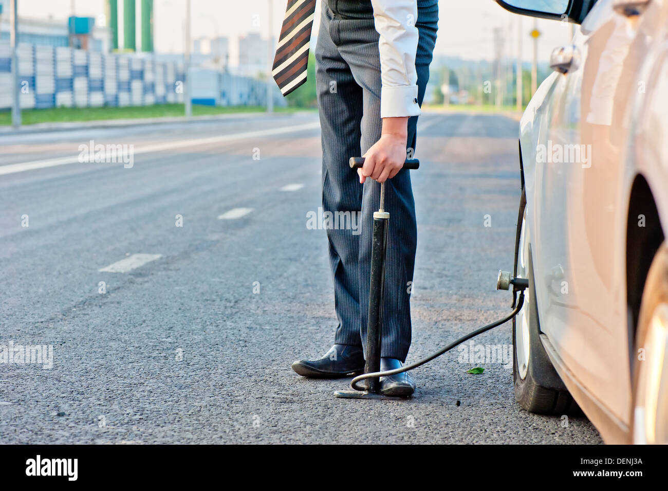 man in a business suit pumps hand pump wheel of a car Stock Photo - Alamy