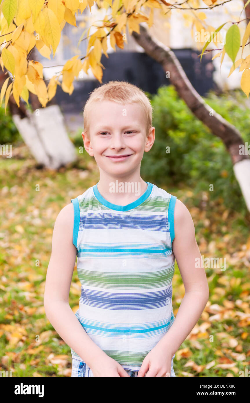 Adorable boy smiling, fall leaves and school building on background ...