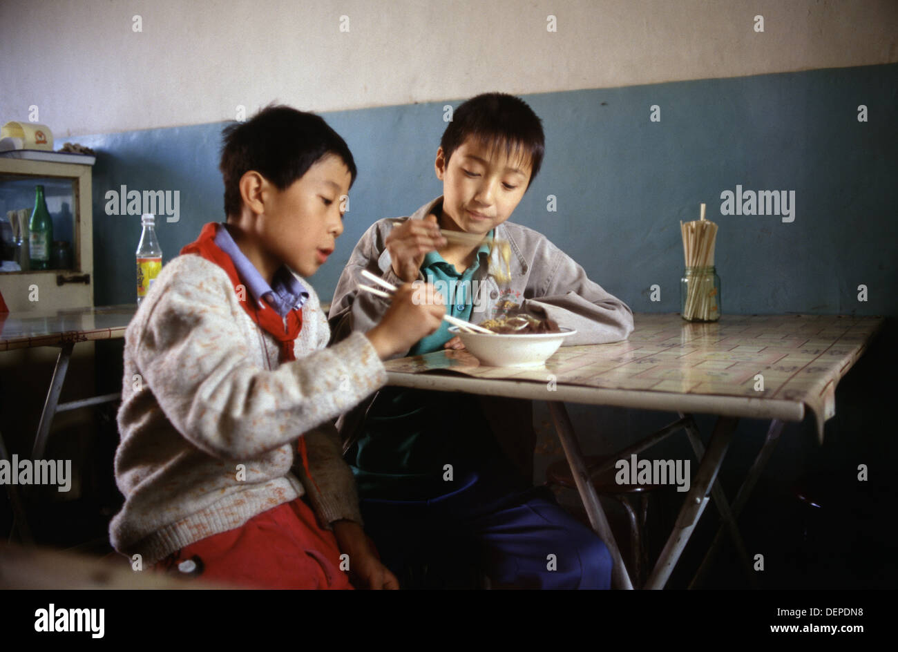 Chinese boys eating noodles with chopsticks in a restaurant in the city ...
