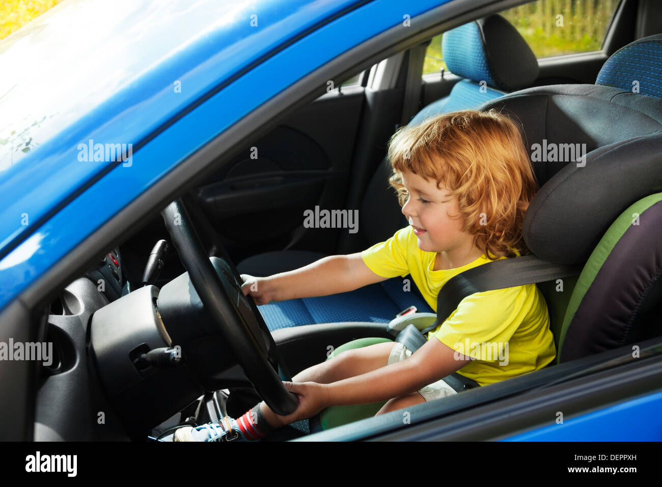 Little boy playing to be a driver in parents car sitting on the first ...