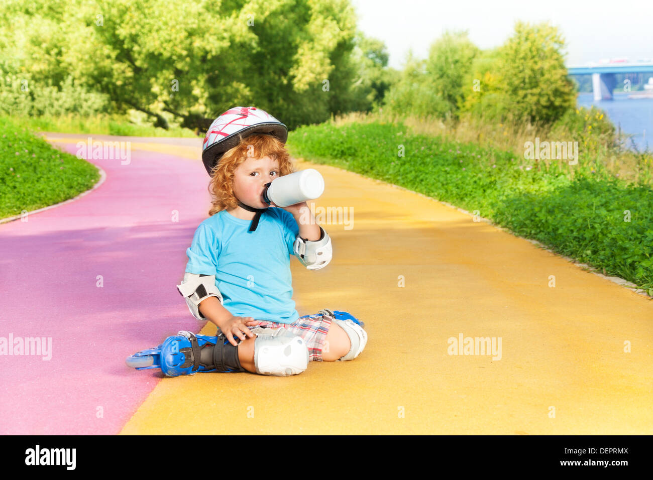 Happy thee years old boy sit with rollerblading and drink water from ...