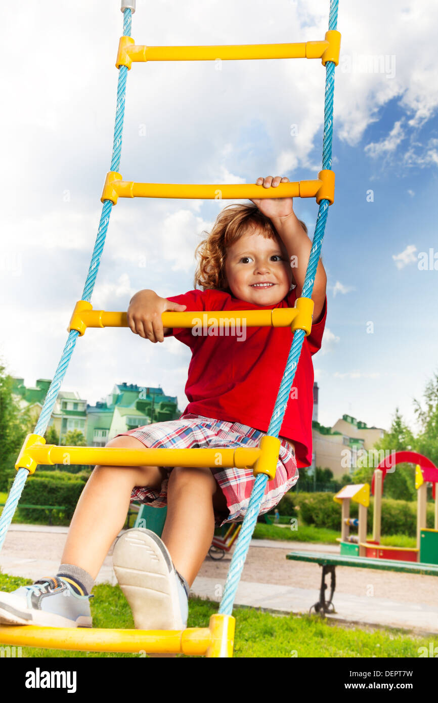 Happy little three years old child boy climbing on the rope ladder with ...