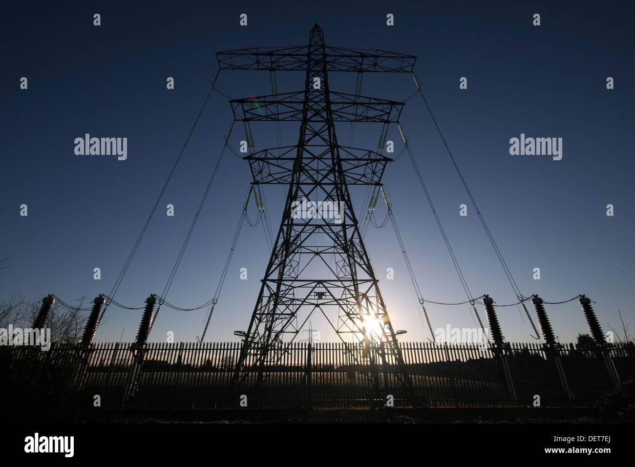 The sun sets behind an enormous electricity pylon Stock Photo - Alamy