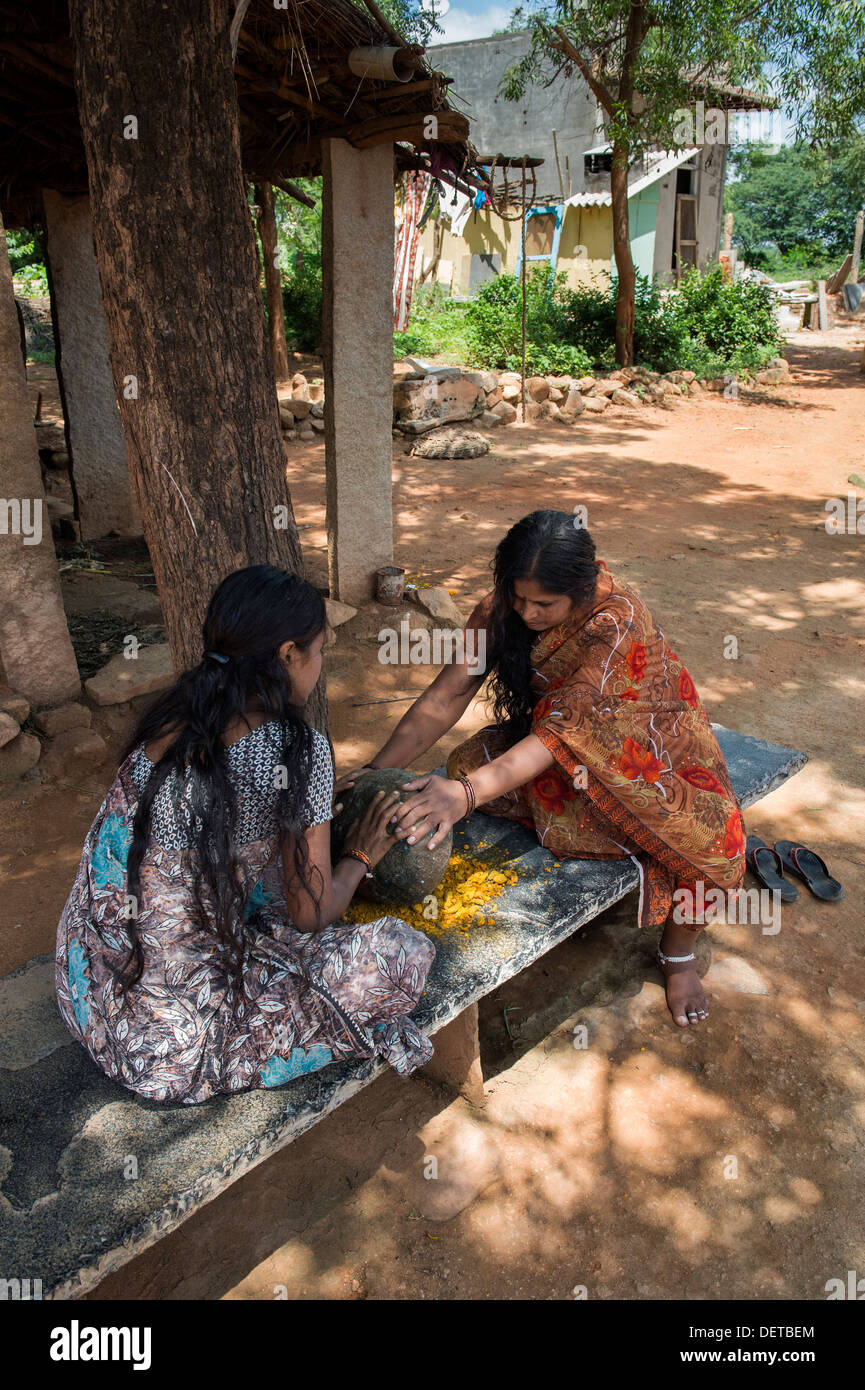 Two Indian women crushing turmeric roots to powder with a round stone ...