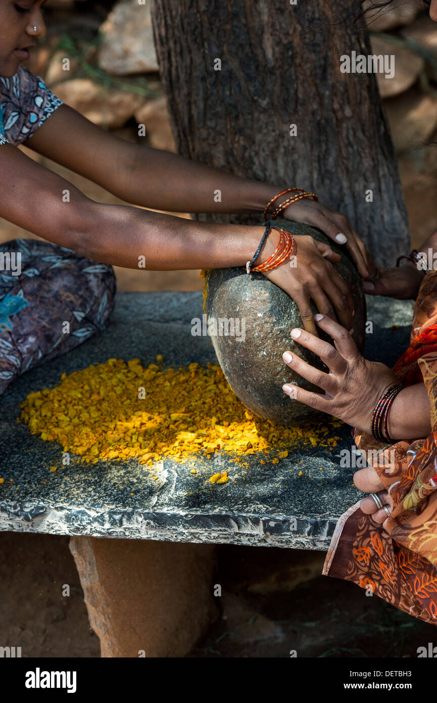 Two Indian women crushing turmeric roots to powder with a round stone ...