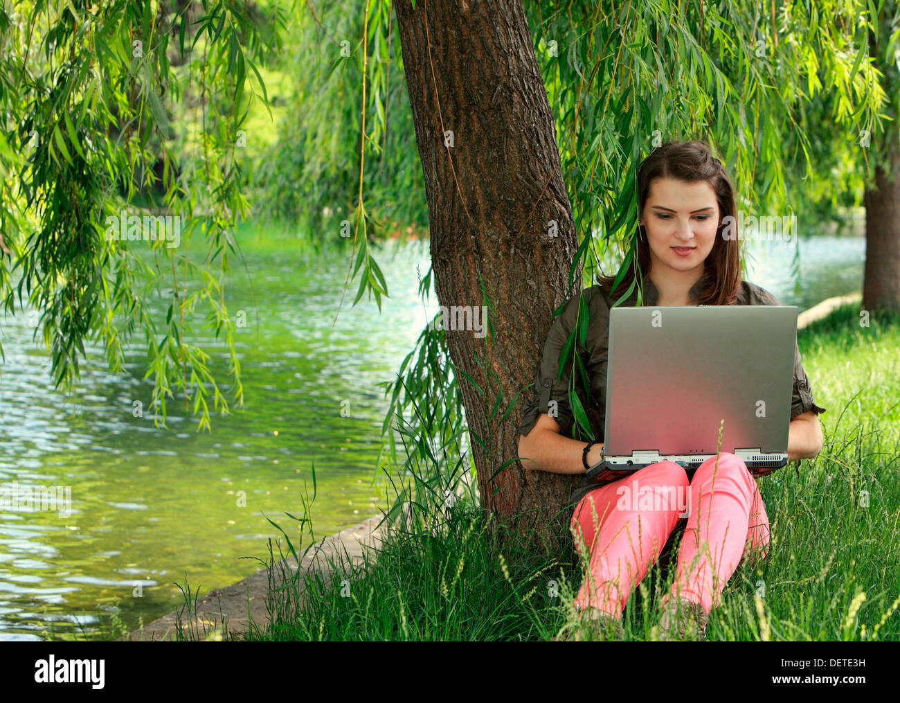 Young pretty woman studying outside in a park under a willow tree, near ...